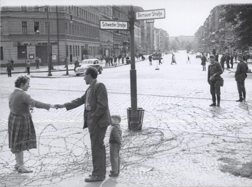 A couple holding hands across a fence of barbed wire as the Berlin Wall ...